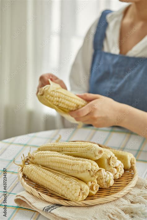 Foto De 테이블에 앉아서 쪄진 찰 옥수수 한개를 집어 찰옥수수 껍질을 까고 있는 모습 Do Stock Adobe Stock