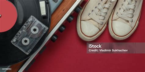 플랫 누워 복고풍 미디어 및 엔터테인먼트 비닐 레코드 오디오 카세트 빨간색 배경에 운동화와 비닐 레코드 플레이어 공간을 복사합니다 80년대 탑 뷰 Dj에 대한 스톡 사진 및