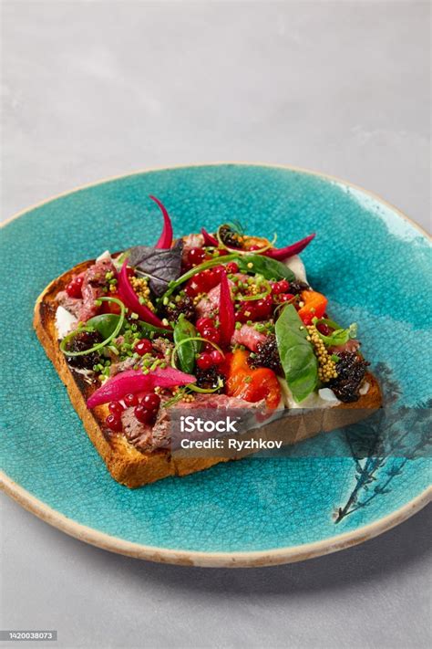 구운 쇠고기 구운 파프리카 양파를 블루 세라믹 접시에 곁들인 브루스케타 구운 쇠고기와 함께 현대적인 스타일로 토스트합니다 현대 세라믹 식기의 셰프 컨셉 브루스케타 수제 디너
