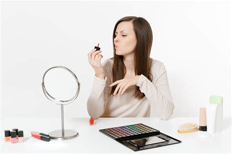 아름 다운 젊은 여 자가 그림을 흰색 배경에 고립 설정된 얼굴 장식 화장품으로 메이크업을 적용 하는 테이블에 앉아 빨간