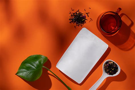 차를위한 흰색 판지 포장 차가있는 오렌지 머그잔 찻잎 및 오렌지색 배경에 Monstera 잎 브랜딩 및 포장 모형 가방에 대한