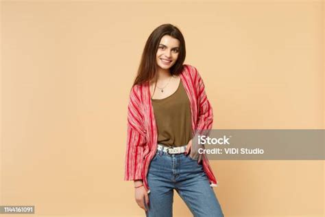 스튜디오에서 파스텔 베이 지 배경에 고립 된 주머니에 손을 잡고 카메라를 찾고 캐주얼 옷에 웃는 젊은 여자의 초상화 사람들은 진심으로 감정 라이프 스타일 개념입니다 복사