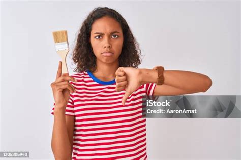 화가 얼굴 엄지 손가락으로 싫어하는 것을 보여주는 부정적인 기호 거부 개념으로 고립 된 흰색 배경 위에 서 브러시를 들고 젊은 브라질 화가 여자 Diy에 대한 스톡 사진 및