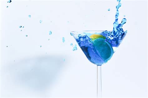 유리에 푸른 액체와 칵테일 물튀김과 방울로 액체를 붓는 푸른 물이있는 유리 흰색 배경에 스플래시와 알코올로 채우는 마티니 유리 상쾌한 음료 컨셉 0명에 대한 스톡 사진 및