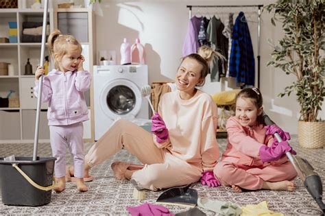 집에서 행복한 가족 어머니와 딸은 집을 청소합니다 젊은 여성과 어린이들은 청소기 걸레 바닥과 청소기를 진공 청소기로 청소합니다 귀여운 작은 도우미 3 명에 대한 스톡 사진