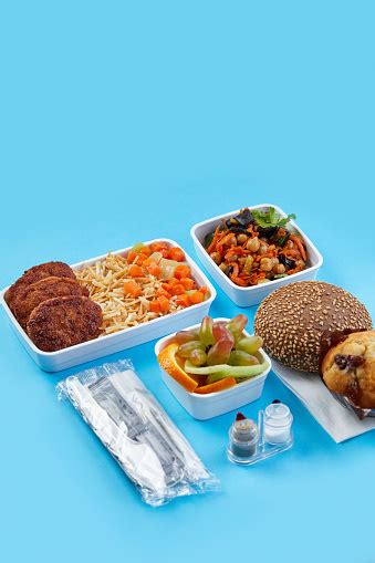 부드러운 파란색 배경에 근접 촬영 일회용 식기 비행기 음식 스낵 일회용 세트 소금과 후추 커틀릿 베이글 롤빵 건포도를 곁들인 과일과 머핀 야채 샐러드가 있습니다 0명에 대한