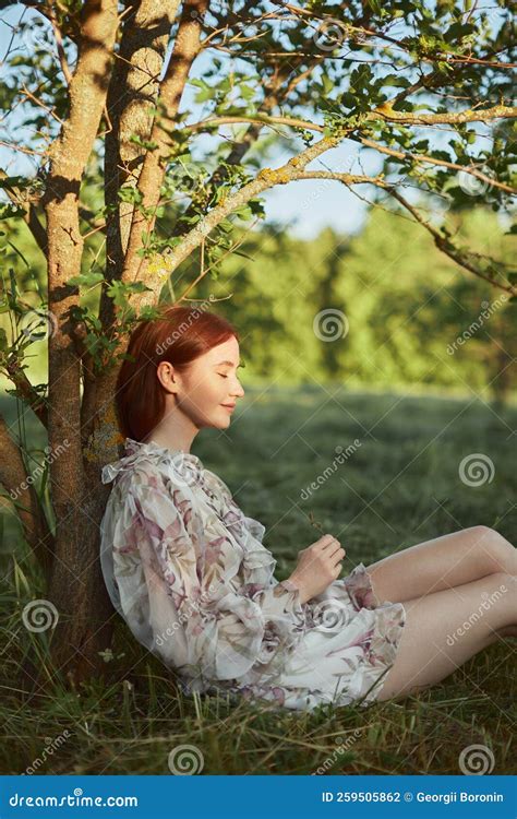 A Girl With Ginger Hair Is Sitting By A Tree With Her Eyes Closed The Enjoyment Of Nature And
