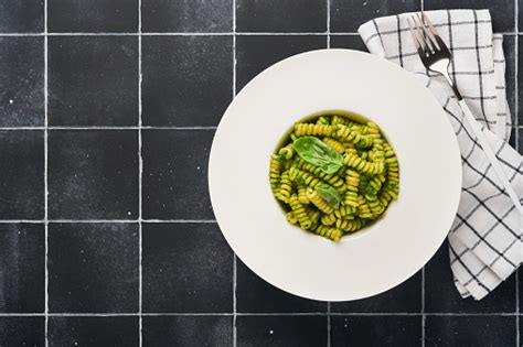 페스토와 이탈리아 푸실리 파스타 검은 돌 조리대 배경에 바질 페스토와 허브 파르 메산 치즈 바질 및 마늘을 흰색 접시에 곁들인 Fusilli 파스타 상단 보기 공간을