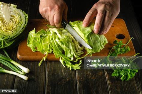 요리사는 신선한 야채와 양파가 들어간 식탁에서 샐러드 용 칼로 신선한 양배추를 자릅니다 어두운 배경에 요리와 레스토랑 또는 호텔 개념 건강한 생활방식에 대한 스톡 사진 및
