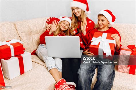 행복한 가족 젊은 어머니와 산타 클로스 모자를 쓴 어린 아이들은 집에서 새해를 축하하고 소파에 앉아 크리스마스 선물을 엽니 다