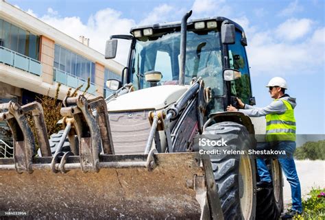 하얀 안전 헬멧과 반사 조끼를 입은 엔지니어가 푸른 하늘을 배경으로 트랙터를 타고 있다 50 54세에 대한 스톡 사진 및 기타