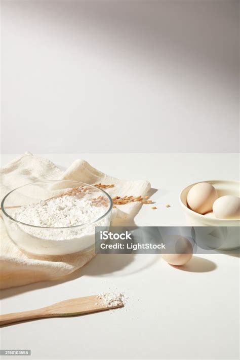 크림 타월에 밀가루 유리 그릇이 있는 최소한의 흰색 배경 둥근 흰색 그릇에 계란 몇 개 격리된 계란 약간의 밀가루가 뿌려진 나무