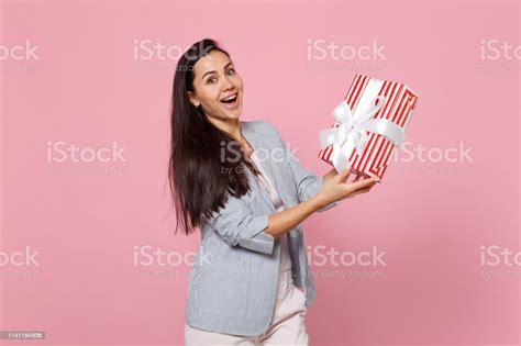 쾌활 한 젊은 여자 분홍색 파스텔 배경에 고립 된 선물 리본 빨간 줄무늬 선물 상자를 들고 세인트 발렌타인 데이 국제 여성의 날 생일 휴일 개념입니다 복사 공간을 모의