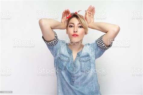 메이크업과 빨간 머리 띠와 함께 캐주얼 블루 데님 셔츠에 재미 있는 아름 다운 젊은 여자의 초상화 서와 토끼 귀 제스처 손