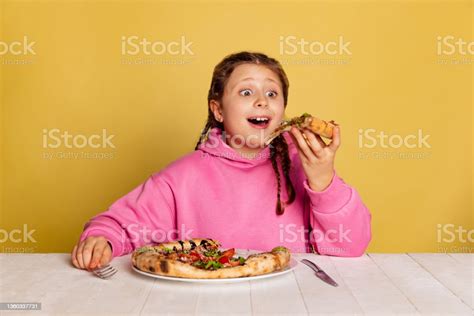 노란 스튜디오 배경에 고립 된 맛있는 이탈리아 피자를 앉아서 시음하는 작은 귀여운 소녀의 스튜디오 샷 노랑에 대한 스톡 사진 및