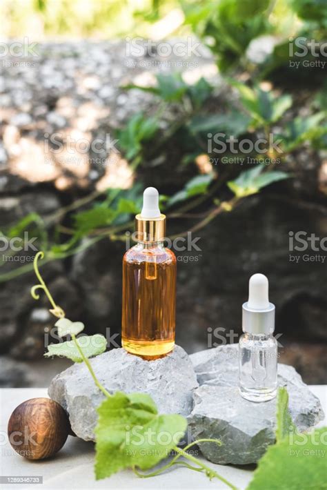 천연 석장 옆에 투명하고 주황색 세럼이 있는 병 자연채광이 있는 포도 잎이 있는 회색 벽에 나무 공 트렌디 한 스타일 포도 추출물 화장품 모형 복사 공간을 참조하십시오