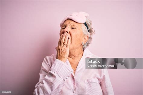 숙 면 마스크와 잠 옷을 입고 선임 아름 다운 여자 고립 된 분홍색 배경 지루 하품 피곤 한 손으로 입을 덮는 불안과 졸음 가리기에 대한 스톡 사진 및 기타 이미지 Istock