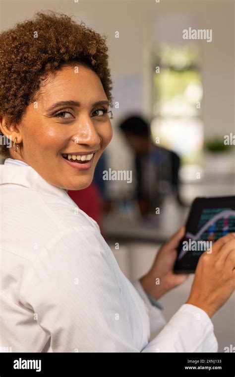 In High School Teacher Holding Tablet And Smiling In Classroom
