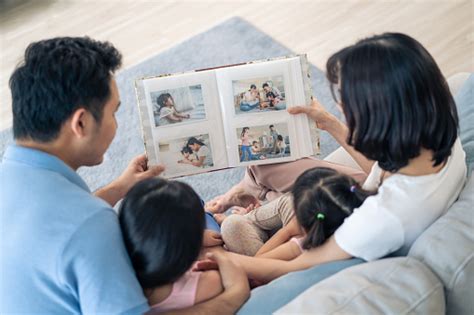 아시아 가족이 오래된 사진 앨범의 사진을 보면 과거를 회상합니다 어린 아이 딸과 함께 앉아 있는 젊은 아름다운 부부는 사진 책의 페이지를 뒤집어 서 관계 기억을 기억하는
