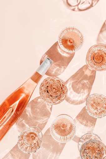 평면도 샴페인 병과 부드러운 분홍색 배경에 로제 와인 잔 예술적 그림자와 태양 눈부심 미적 정물화 크리스탈 와인 잔 여름 파티를위한 스파클링 음료 Copyspace 그림자에