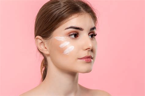 아름다운 모델은 분홍색 배경 위에 고립 된 히알루론산 크림의 흰색 튜브를 들고 피부에 보습 화장품을 적용합니다 미용 및 건강 치료의 개념 갈색 머리에 대한 스톡 사진 및