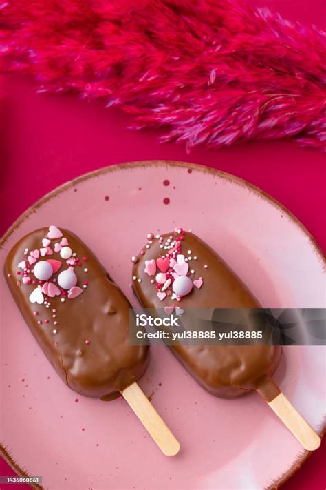 초콜릿 크림을 곁들인 컵케이크 아이스크림 초콜릿 컵케이크는 자홍색 배경에 말린 꽃이 있는 분홍색 접시에 놓여 있습니다 위에서 본 모습 아이스크림의 형태로 막대기에 초콜릿