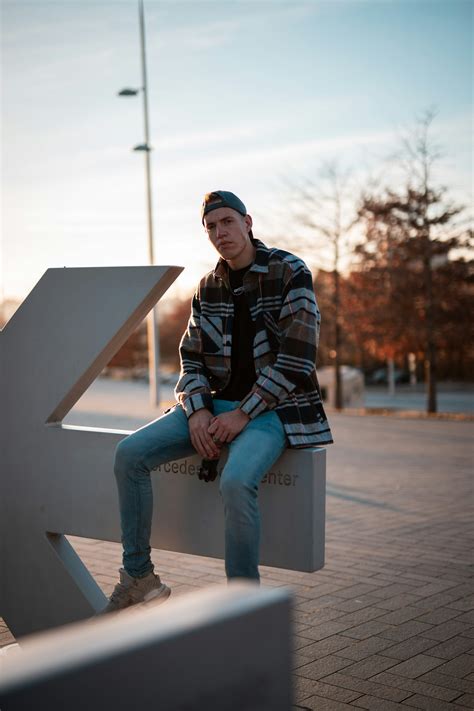 흑백 격자 무늬 드레스 셔츠와 파란색 데님 청바지를 입은 남자가 흰색 콘크리트에 앉아 있다 사진 Unsplash의 무료 슈투트가르트 이미지