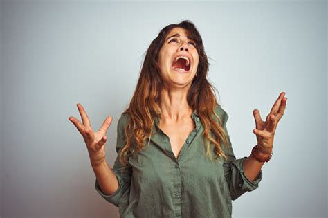 회색 고립 된 배경 에 서 녹색 셔츠를 입고 젊은 아름다운 여자는 미친 미친 소리와 공격적인 표정과 팔을 제기 고함 좌절 개념입니다 갈색 머리에 대한 스톡 사진 및 기타