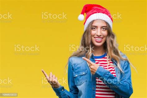 아름 다운 젊은 금발 여자 웃 고 옆에 두 손과 손가락으로 가리키는 카메라 보고 격리 된 배경 위에 크리스마스 모자를 쓰고 가리키기에 대한 스톡 사진 및 기타 이미지