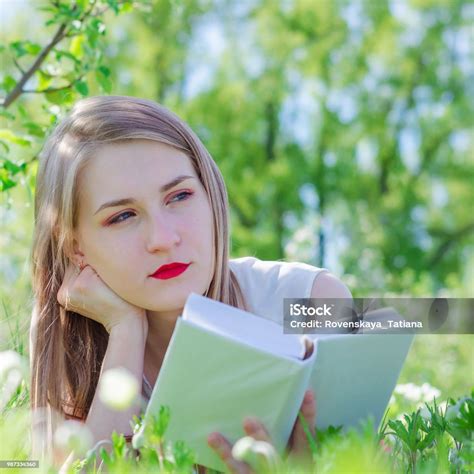 긴 머리를 가진 백색 탑에 근접 젊은 예쁜 여자는 화창한 날에 꽃 사과 나무 정원 및 읽기 책에 둘러싸인 풀밭에 놓여 있습니다 텍스트에 대 한 공간을 복사 개화기에 대한