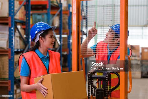 지게차 트럭에서 창고 창고의 선반 팔레트로 제품이나 소포 제품을 옮기거나 옮기는 창고 노동자 그룹 안전 조끼를 입은 아시아 남성과 여성 노동자 창고에서 일하는 헬멧 상점에