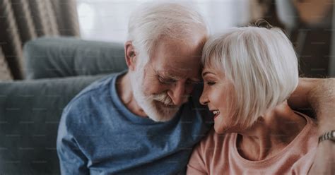 모든 연령대의 사랑과 텐던스 소파에서 함께 시간을 즐기면서 부드러운 이마를 만지는 행복한 미소를 짓는 회색 머리 남자와 여자의 초상화를 닫습니다 사진 Unsplash