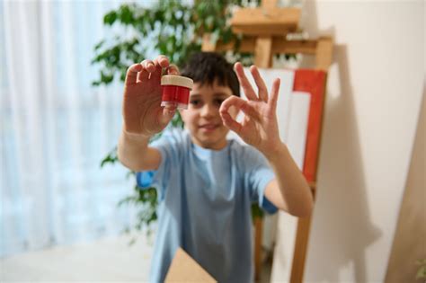 빨간 구아체 페인트를 들고 집에서 나무 이젤에 캔버스에 서 카메라를 보고 Ok 사인을 보여주는 초점 검은 머리 학교 백인 소년 소년 예술가의 손에 초점을 맞춥니다 8 9