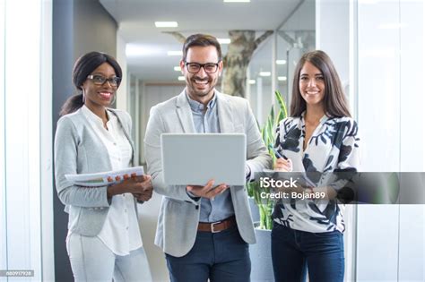 노트북과 종이 문서 사무실 복도에 서 서 카메라를 보고 있는 3 명의 성공적인 사업 사람들의 그룹 기업 비즈니스에 대한 스톡 사진 및 기타 이미지 Istock