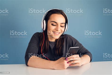 아름 다운 젊은 여자의 초상화는 웃 고 재미 있는 파란 벽 앞에 휴대 전화를 사용 하 여 집에서 음악을 듣고 가정 생활에 대한