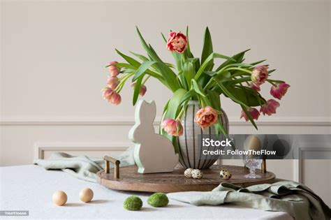화려한 부활절 달걀 부활절 토끼 조각품 튤립이 달린 꽃병 나무 흔적 치장 벽토가있는 베이지 색 벽 회색 암탉 및 개인 액세서리가있는 부활절 식당의 인테리어 디자인 가정 장식
