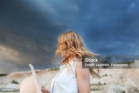 바다와 수평선의 배경에 바람에 긴 흐르는 금발 머리를 가진 젊은 여성의 다시 보기 해변과 뇌우 하늘 배경을 따라 걷는 아름다운 소녀 외로움과 슬픔 개념 건강한 생활방식에