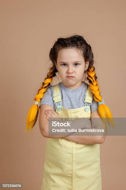 노란 카네칼론 피그테일을 입은 작은 백인 소녀는 누군가가 화를 내고 흰색 배경에는 노란 점프수트와 회색 티셔츠를 접은 채 분노를 표출했습니다 땋은 머리에 대한 스톡 사진 및