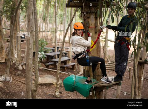 Happy Woman Leaning On Zip Line While Man Standing On Wooden Platform Holding Rope In The Forest