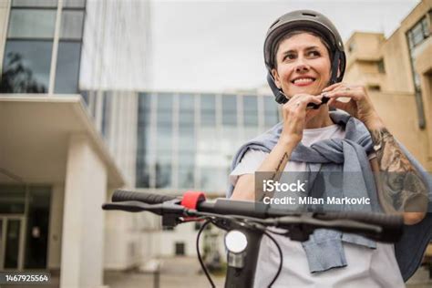 현대 비즈니스 여성이 전기 스쿠터를 타고 일하러 와서 그녀가 일하는 사무실 건물을지나갑니다 전기 연료 및 전력 생산에 대한 스톡 사진 및 기타 이미지 Istock