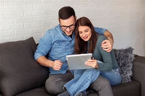 젊은 부부는 방에서 온라인 쇼핑에 시간을 보내는 손에 태블릿과 신용 카드와 소파에 앉아 Brand Name Mobile Payment에 대한 스톡 사진 및 기타 이미지
