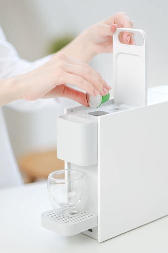 한 여성이 커피 카풀라를 손에 들고 캡슐 커피 머신에서 에스프레소를 준비합니다 흰색 배경 밝은 방 인간 손에 대한 스톡 사진 및