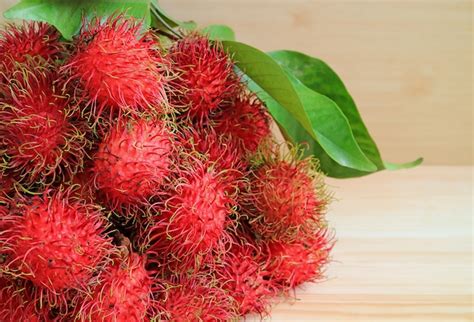 Premium Photo Bunch Of Fresh Ripe Rambutan Fruits With Green Leaves On The Wooden Table