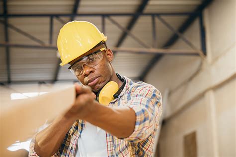 아프리카계 미국인 목수가 작업장에서 나무 널빤지를 나르면서 나무 조각을 검사하고 있습니다 건설 작업 목재 품질 검사 및 목공 장인 정신 30 34세에 대한 스톡 사진 및