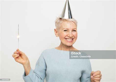 촛불과 스파클러와 컵 케이크와 함께 생일을 축하하는 원뿔 모자를 쓰고 있는 행복한 중년 여성 60 64세에 대한 스톡 사진 및