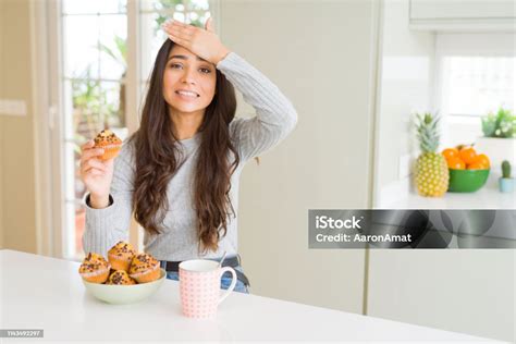 초콜릿 칩 머핀 및 마시는 커피를 먹는 젊은 여성은 머리에 손으로 스트레스 수치심과 깜짝 얼굴 충격 화가 좌절 두려움과 실수에 대 한 화가 먹기에 대한 스톡 사진 및 기타