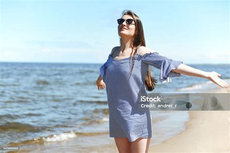 두 손을 벌리고 서 있는 바다 해변에서 자유로운 행복을 누리고 있는 행복한 미소 짓는 여자 여름 드레스를 입은 갈색 머리 여성 모델의 초상화는 야외 휴가 휴가 동안 자연을