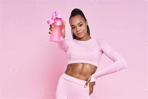 Confident African Woman In Sports Clothing Showing Bottle With Water Against Pink Background