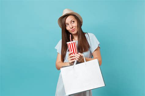 초상화 꽤 유행 웃는 소녀 여름 드레스 밀 짚 모자 쇼핑 후 구매와 패키지 가방을 들고 소 다 물 컵 블루 파스텔 배경에 고립 광고에 대 한 공간을 복사 가방에 대한 스톡