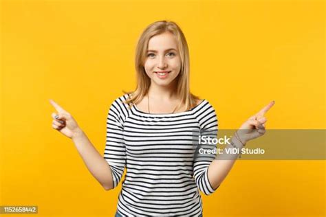 스튜디오에서 노란 주황색 벽 배경에 고립 된 인덱스 손가락을 가리키는 줄무늬 옷에 아름 다운 젊은 여자의 초상화 사람들은 진심으로 감정 라이프 스타일 개념입니다 복사 공간을